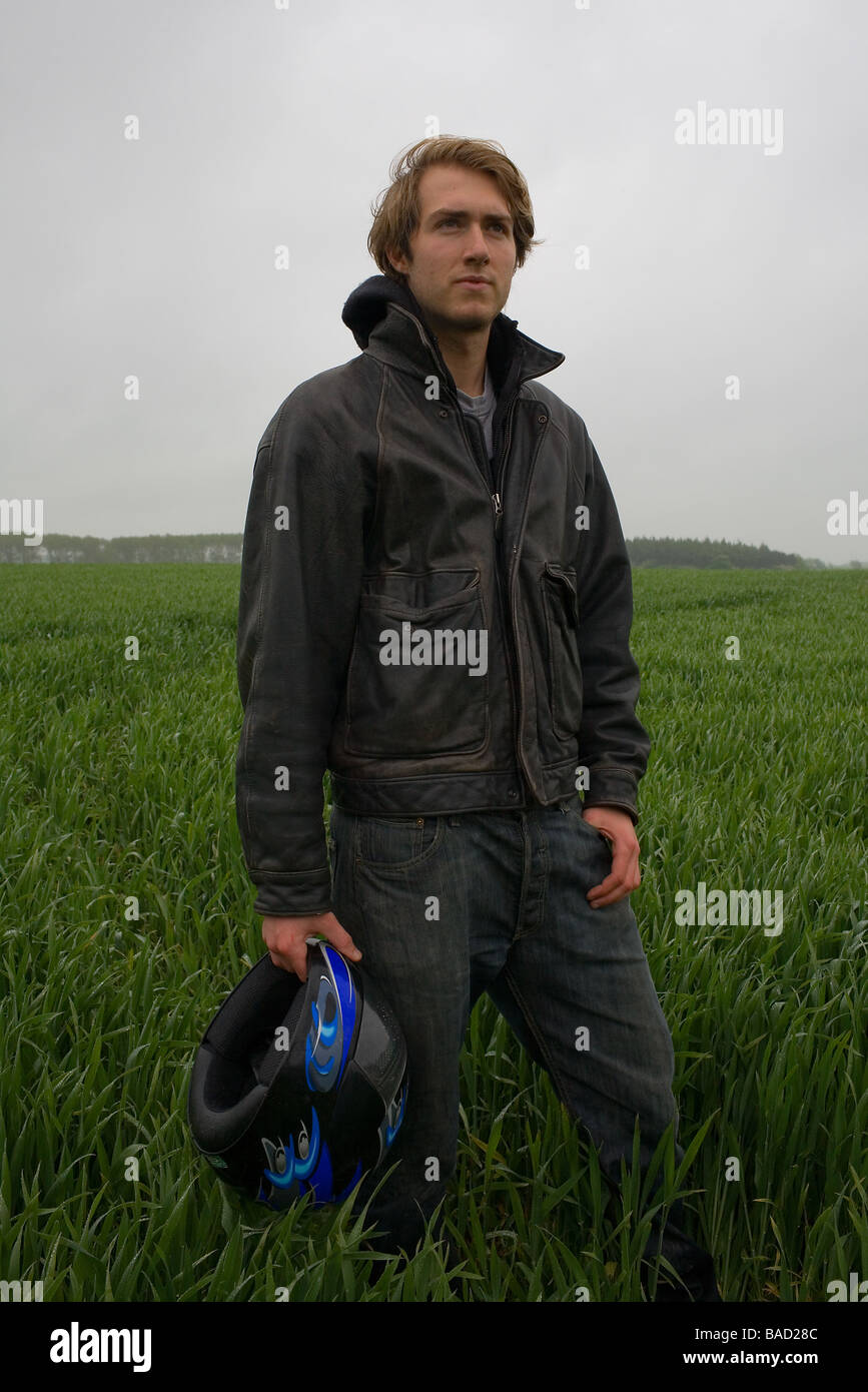 A young man wearing a black leather jacket holding a motorcycle helme ...