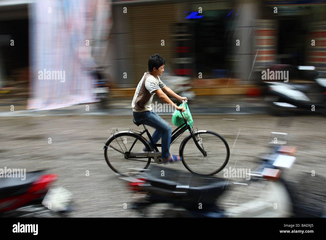 Panning. Street scene. Man riding his bicycle under the rain in Hanoi ...