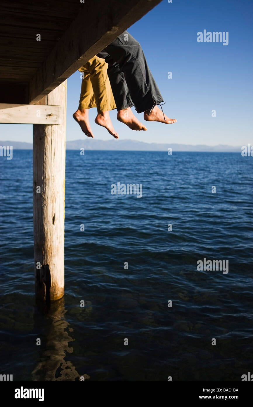 Women Dangling Feet from Dock over Lake Stock Photo - Alamy