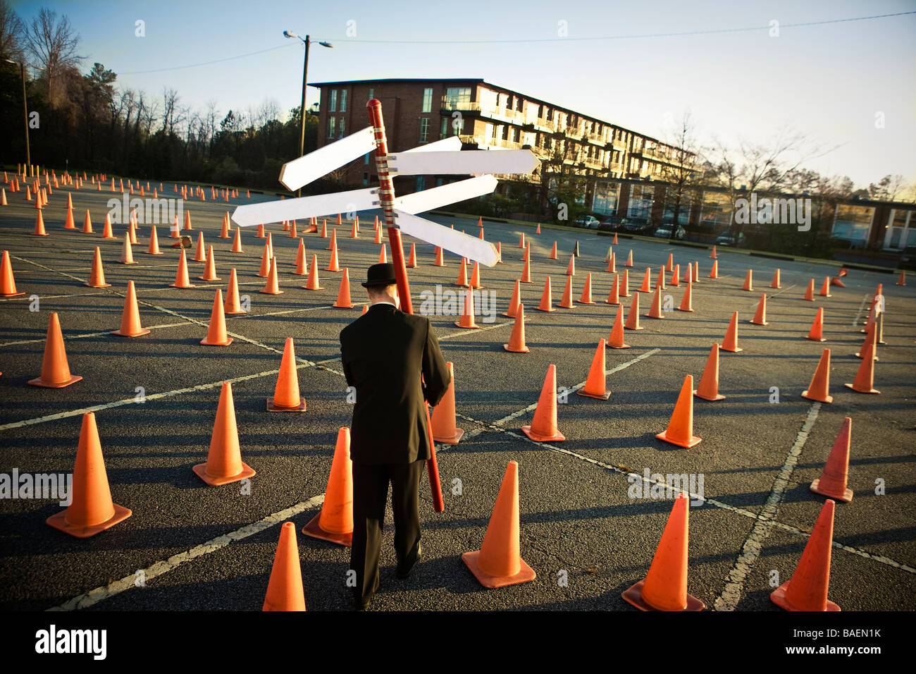 a man with a directional sign walks through a maze of traffic cones ...