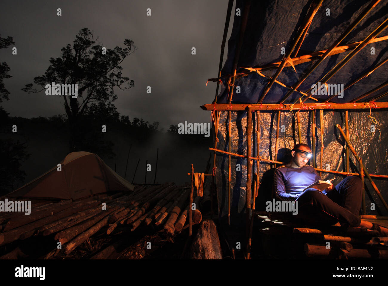 Male cave explorer reads a book late at night in his remote jungle camp ...