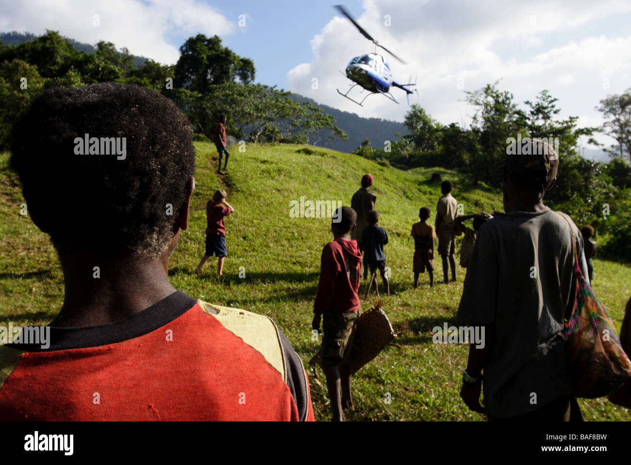 Local tribesmen watch on as a helicopter lands bringing in a team of ...