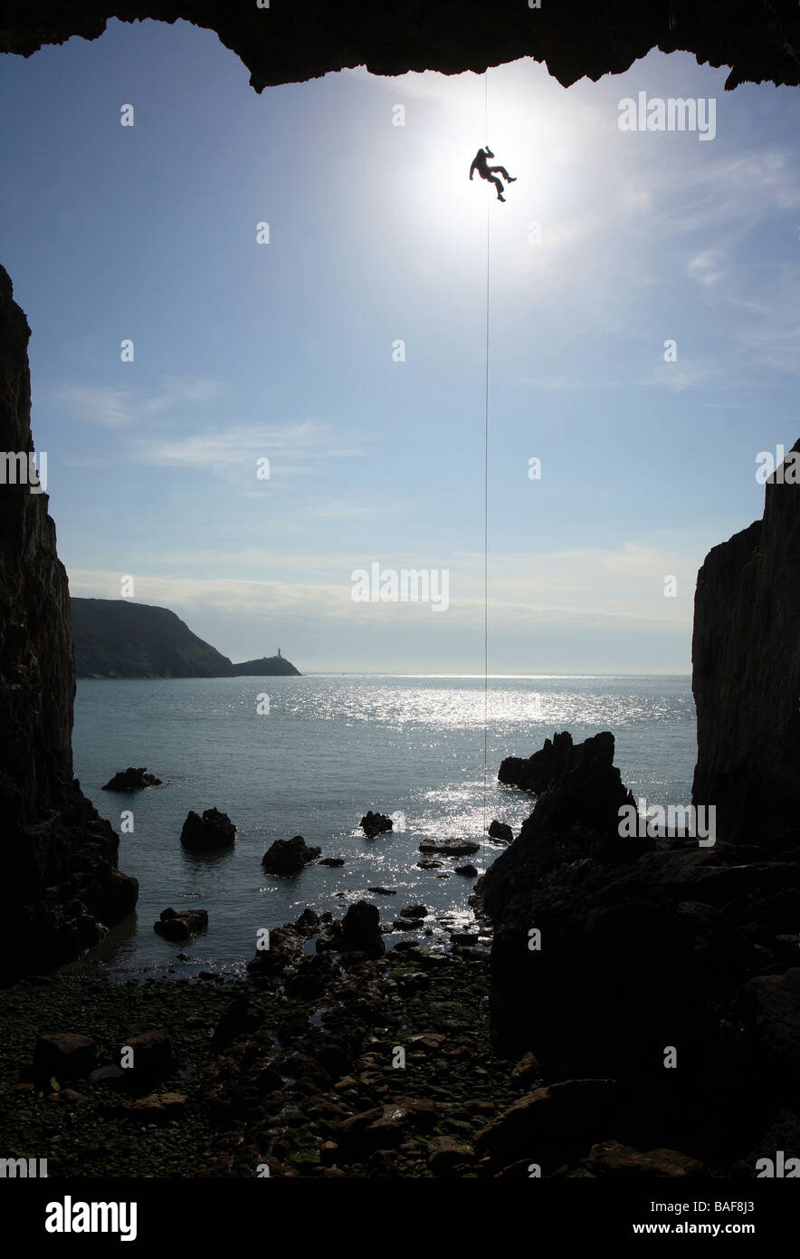Climber ascending a rope out of a cave on the west coast of Wales Stock ...