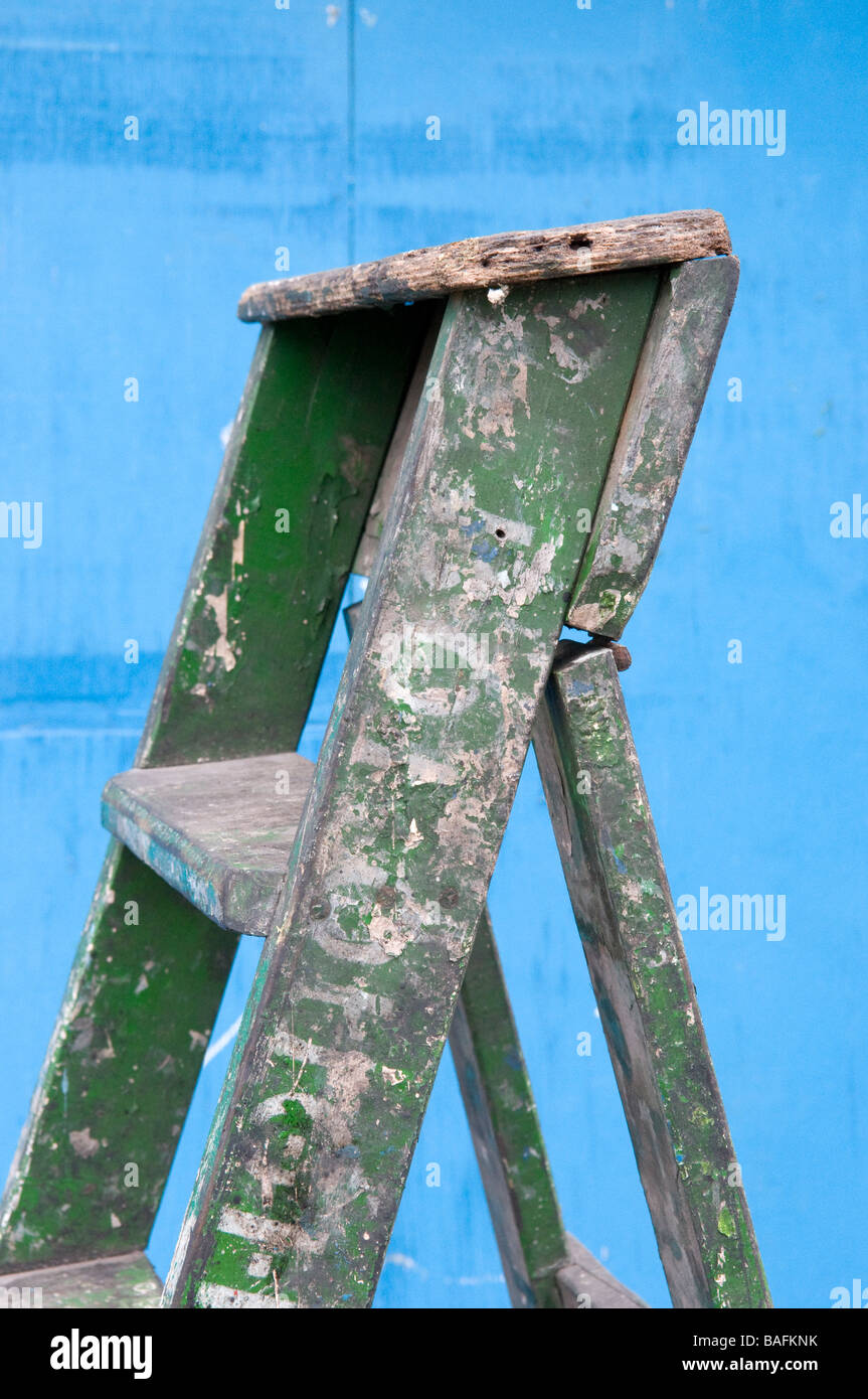 Old green wooden ladder with paint marks against blue door background ...