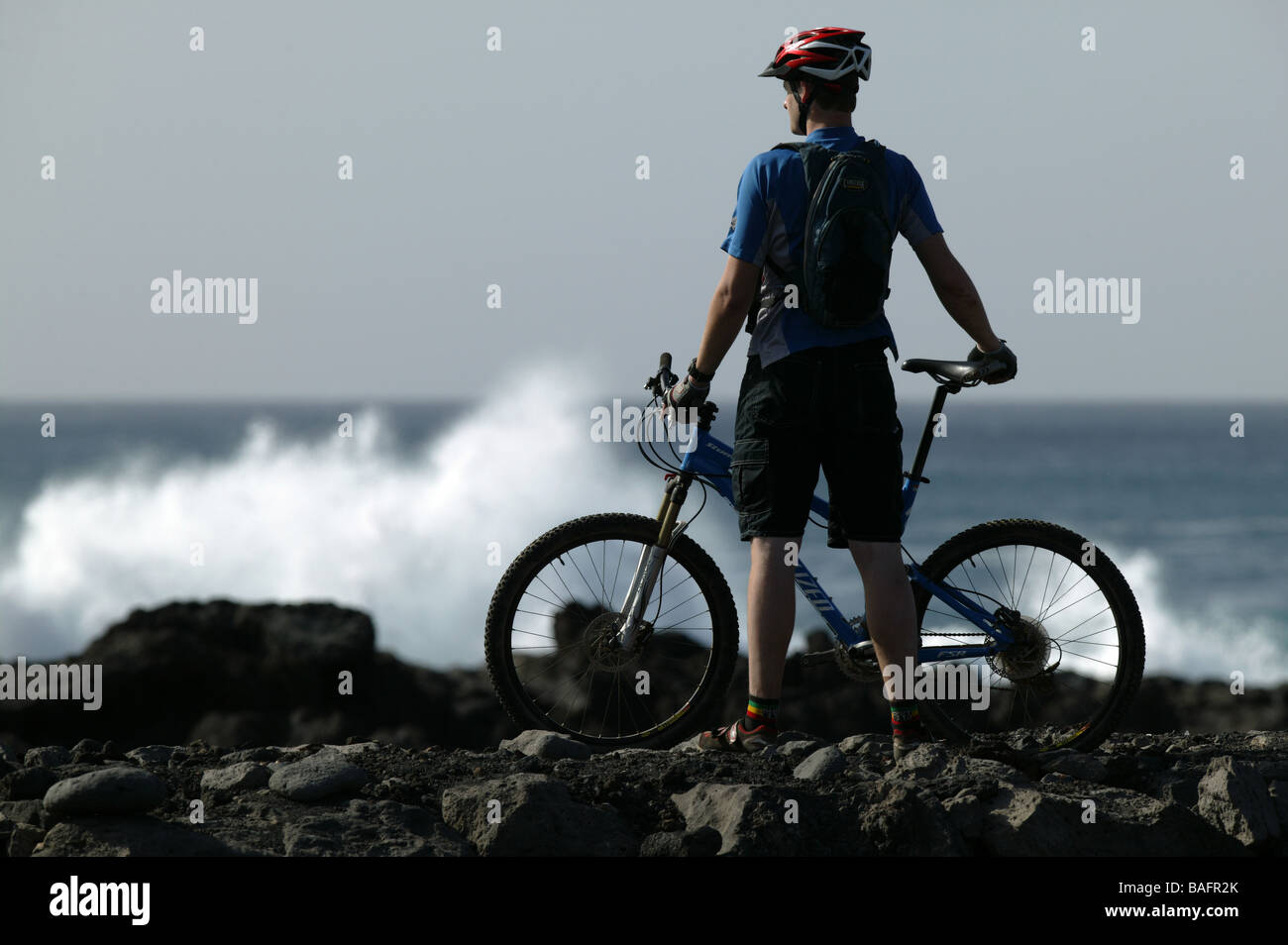 A Mountain Biker watches waves crash on a shoreline Stock Photo - Alamy