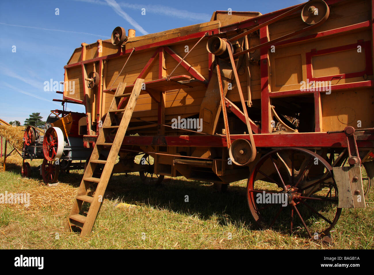 An old French belt driven threshing machine painted in yellow and red ...