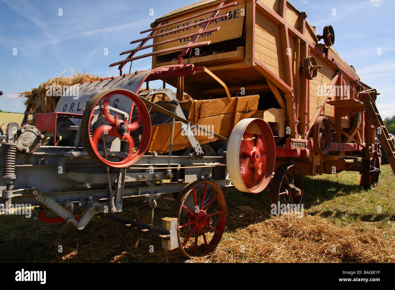An old French belt driven threshing machine painted in orange in a ...
