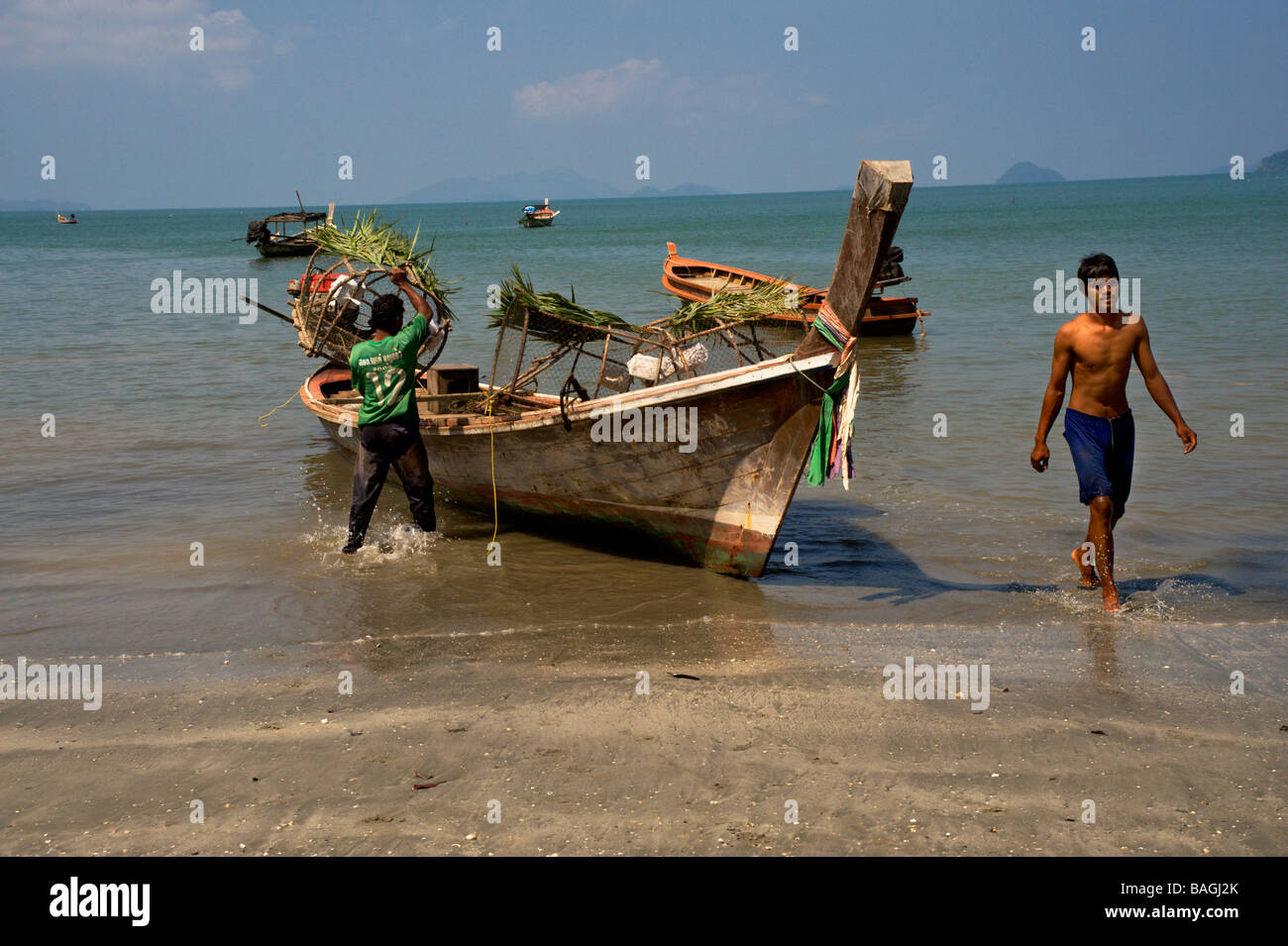 Young man loading fish traps into a long tail boat in south Thailand ...