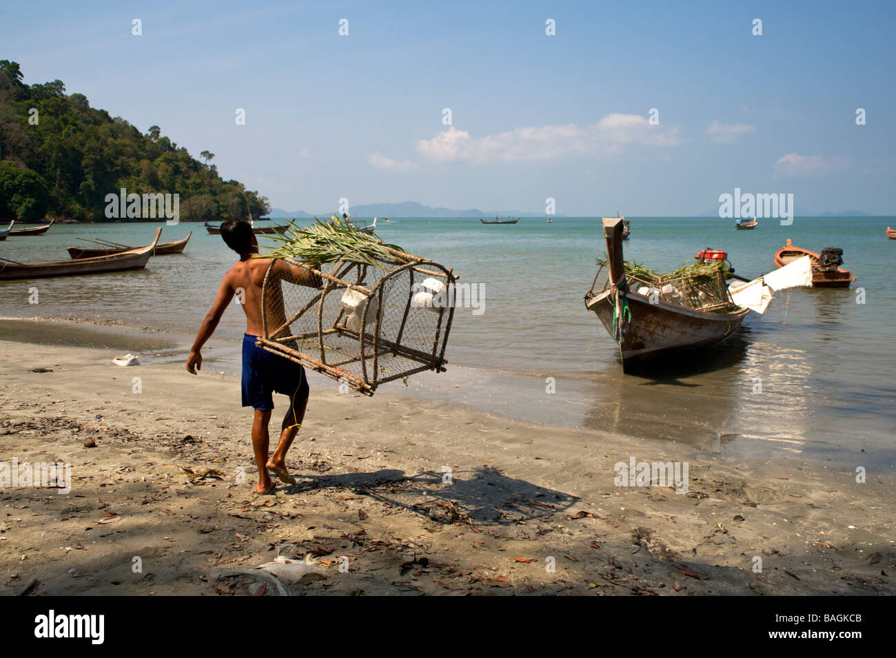 Young man loading fish traps into a long tail boat in south Thailand ...