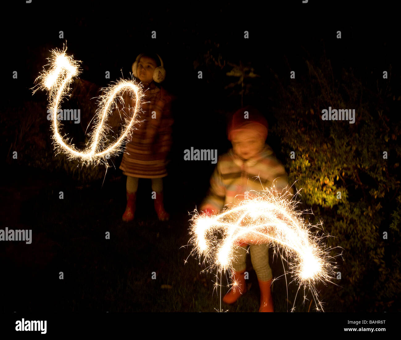Two young girls swirl sparklers around in their back garden on bonfire ...