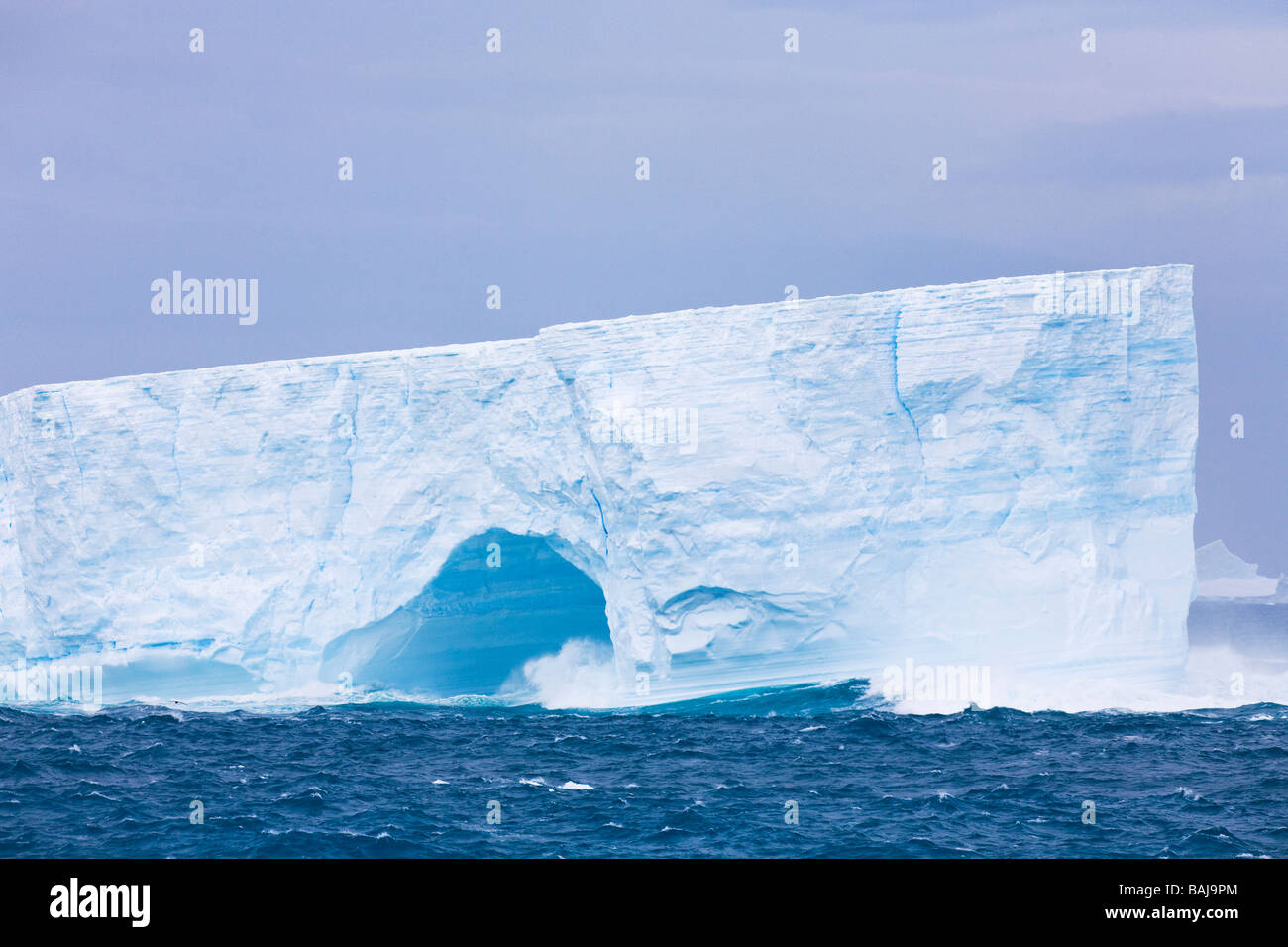 Ice arch in blue tabular iceberg in stormy weather Southern Ocean ...