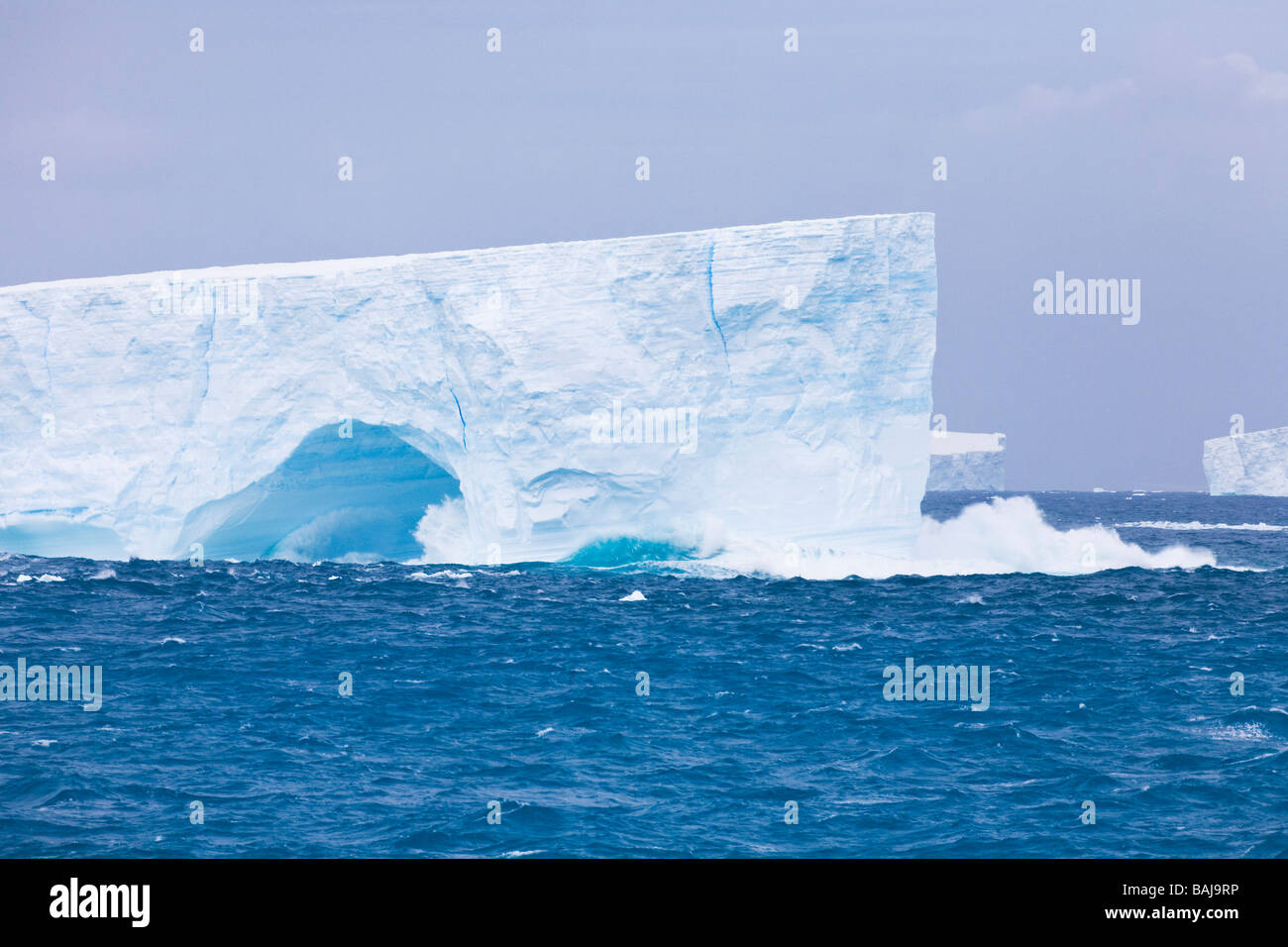 Ice arch in blue tabular iceberg in stormy weather Southern Ocean ...