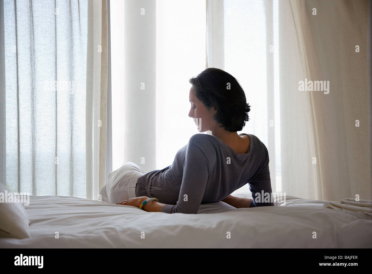 Woman reclining on bed in bedroom Stock Photo - Alamy