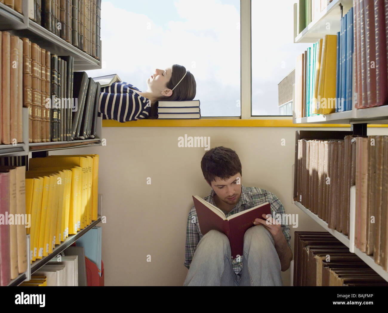 Female student lying down on library windowsill, male student sitting ...