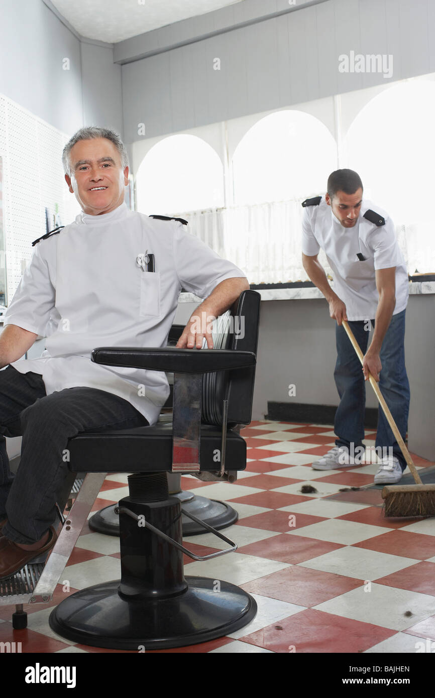 Two barbers in barber shop, one sweeping floor Stock Photo - Alamy