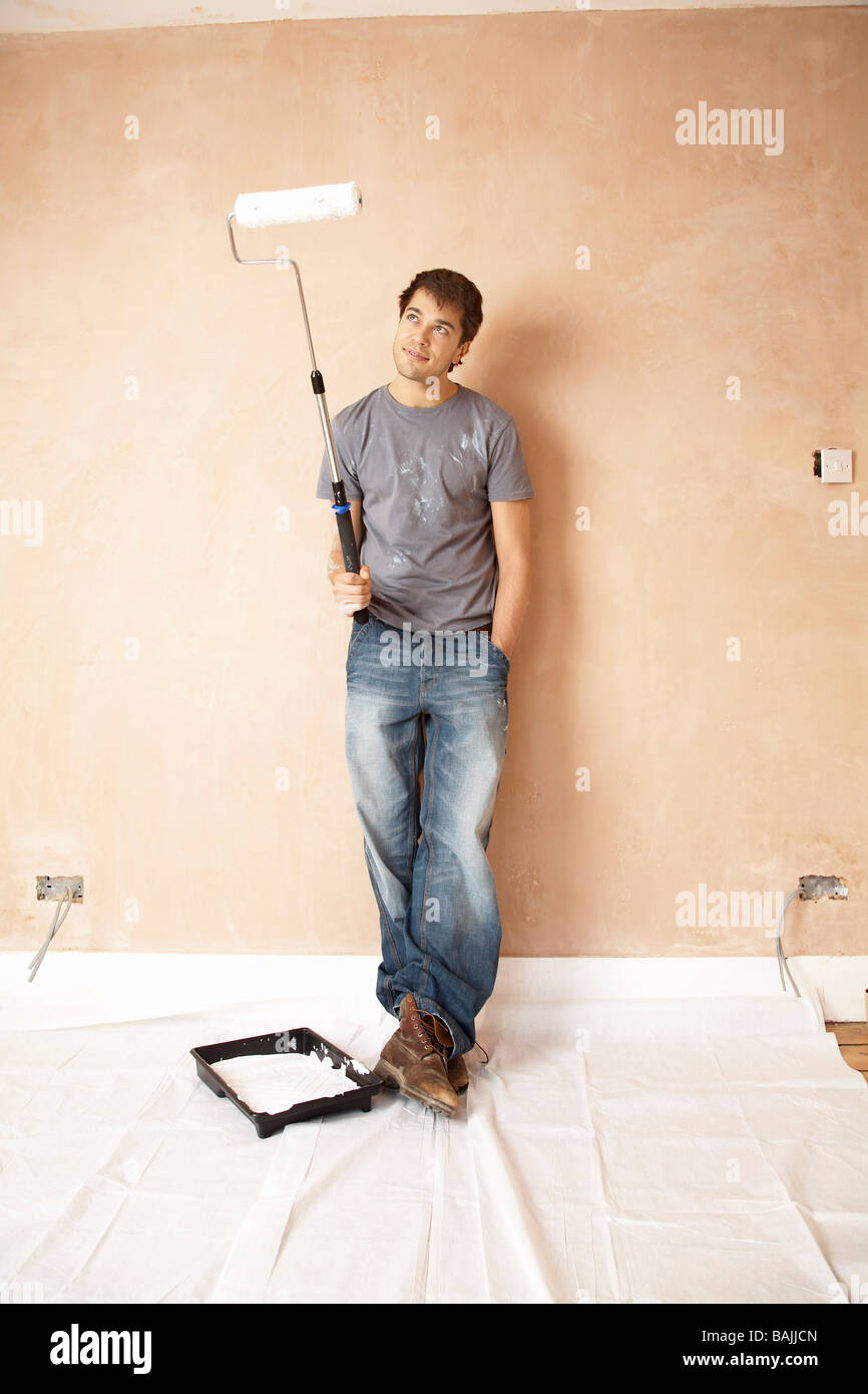 Man standing with paint roller in unrenovated room, portrait Stock ...