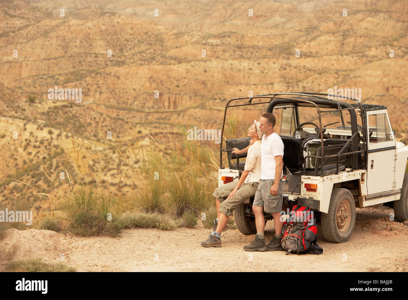 Couple sitting in back of four wheel drive car on cliff edge in desert ...