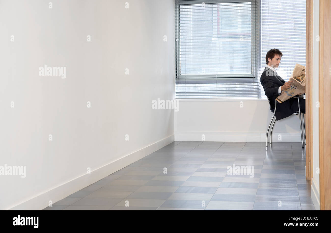 Businessman sitting in empty room reading newspaper, side view Stock ...