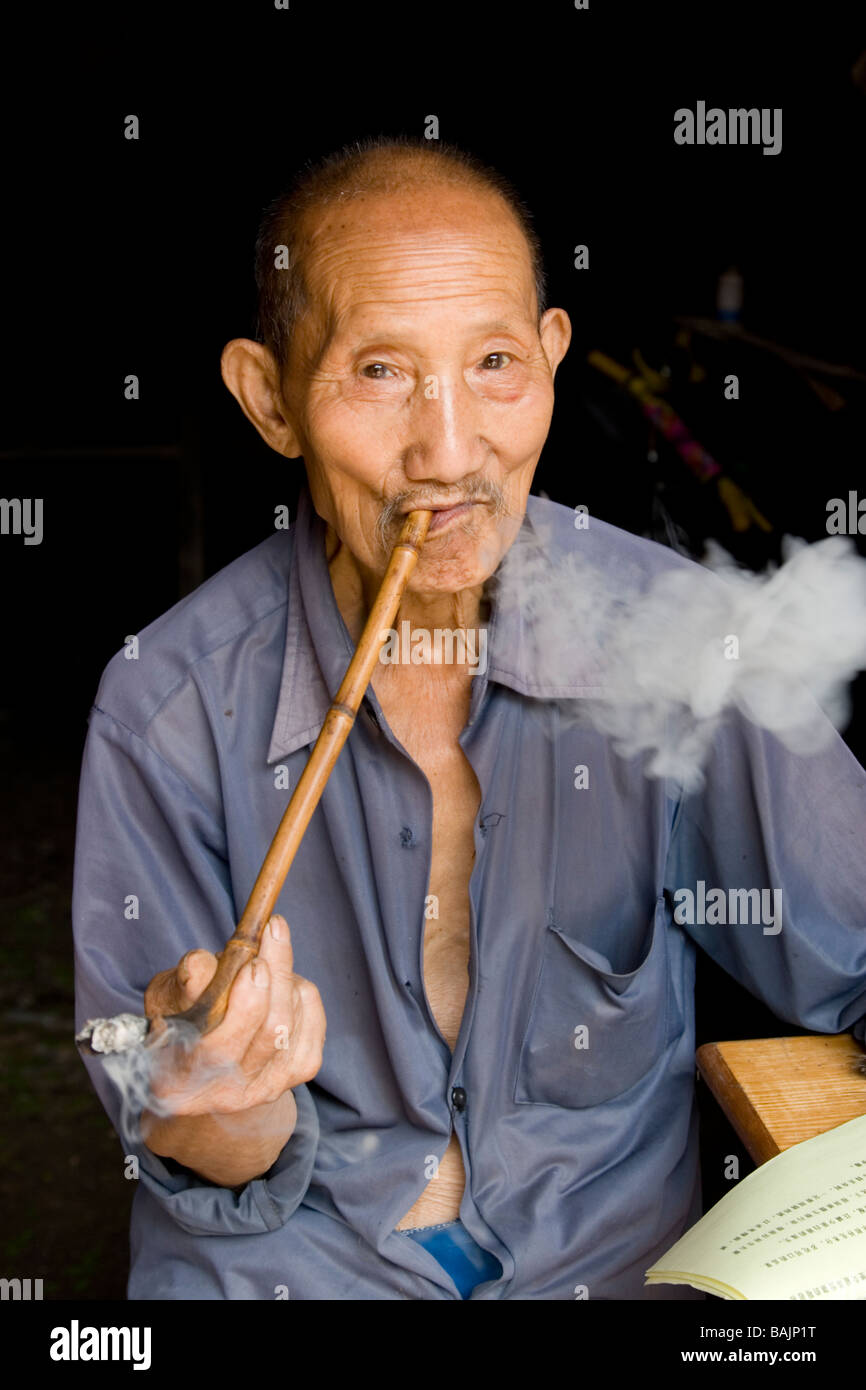 An Old Man In The Courtyard Of His Farmhouse Smoking Home Made Pipe And
