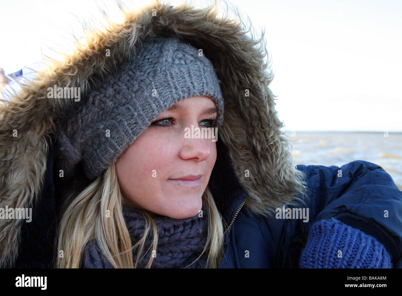 pretty young girl,wrapped up warm, staring out over the cold water ...