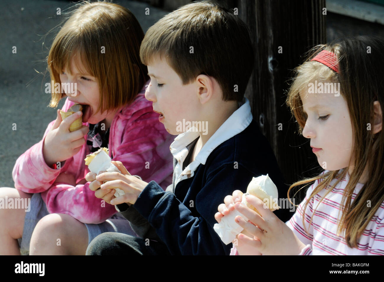 Three kids boy and two girls eating and enjoying ice cream cones and ...