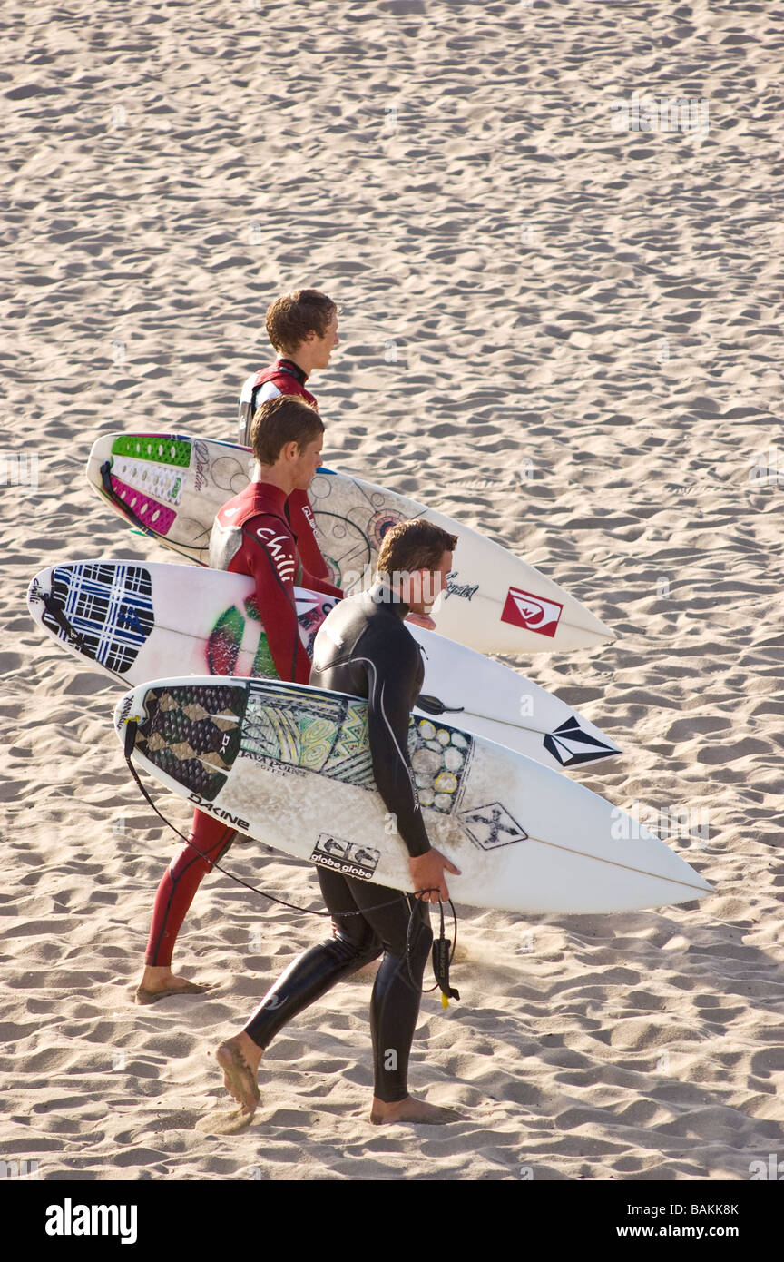 Three surfers with their surf boards exiting the water in Huntington ...