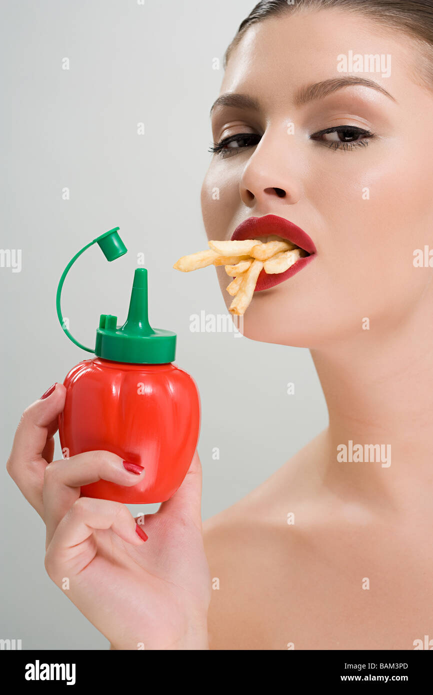 Woman holding tomato ketchup and eating fries Stock Photo - Alamy