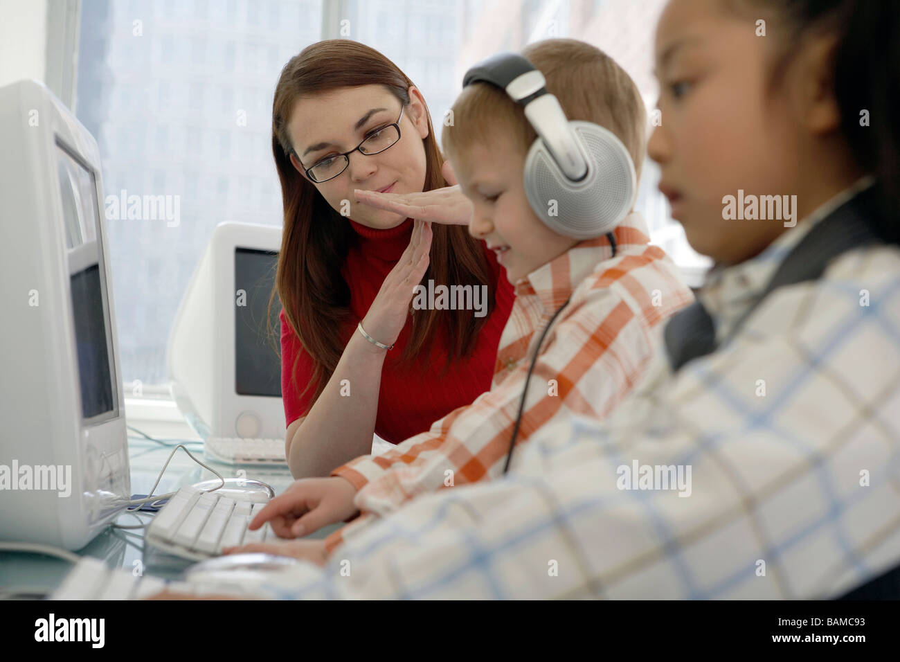 Teacher Signaling Next To Children Using Computers Stock Photo - Alamy