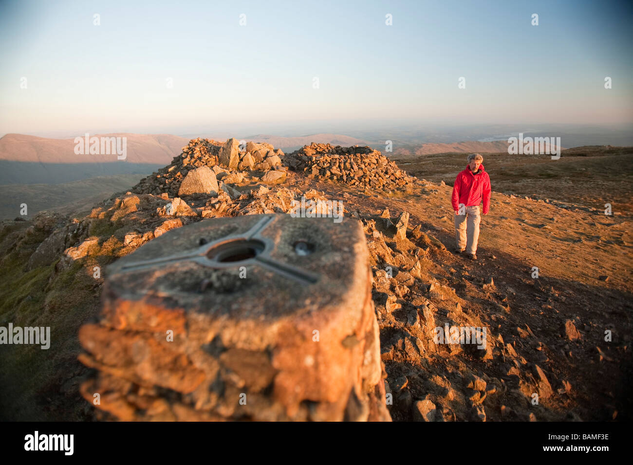 A walker on the summit of Red Screes at sunset in the Lake District UK ...
