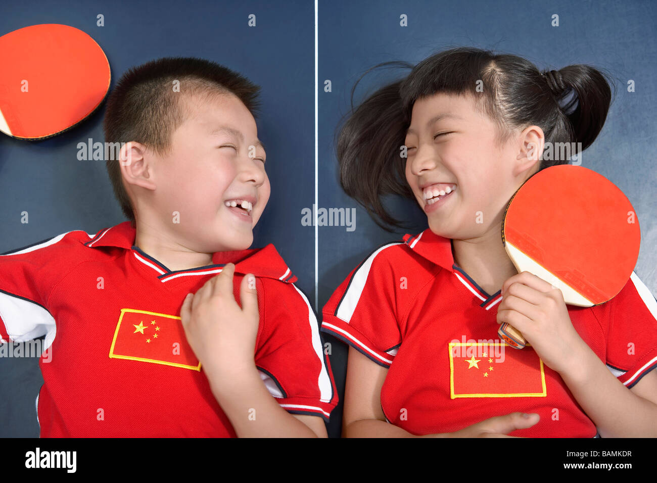 Children Lying Down, Laughing And Holding Table Tennis Rackets Stock ...