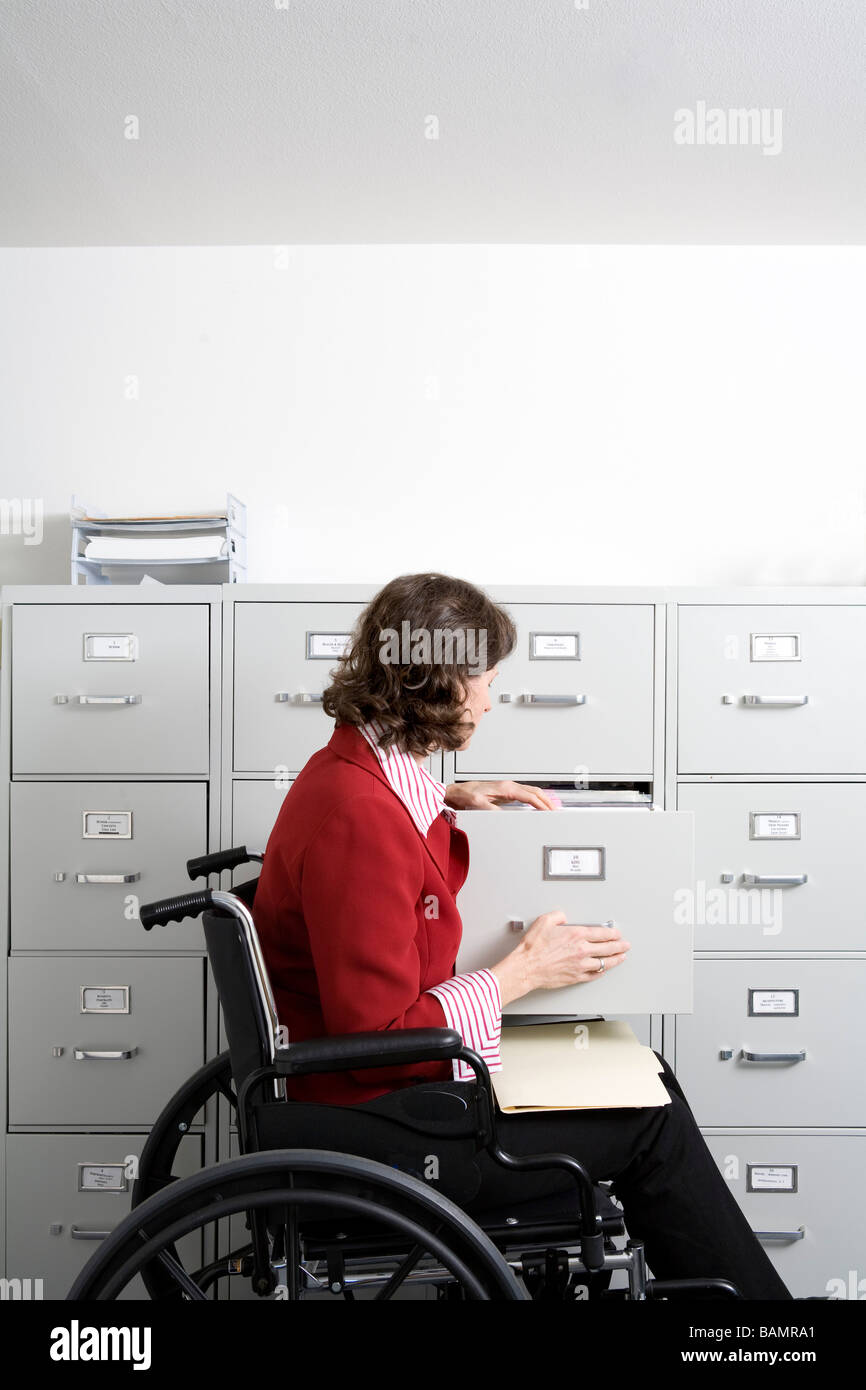 Woman in a wheelchair opening drawer on file cabinet Stock Photo - Alamy