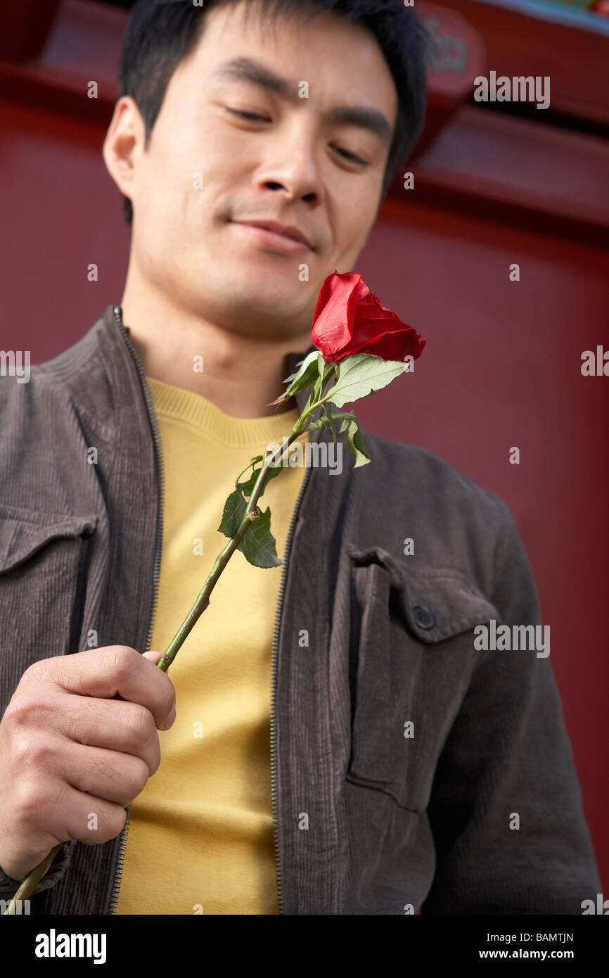 Young Man Standing Outdoors Admiring A Red Rose Stock Photo - Alamy