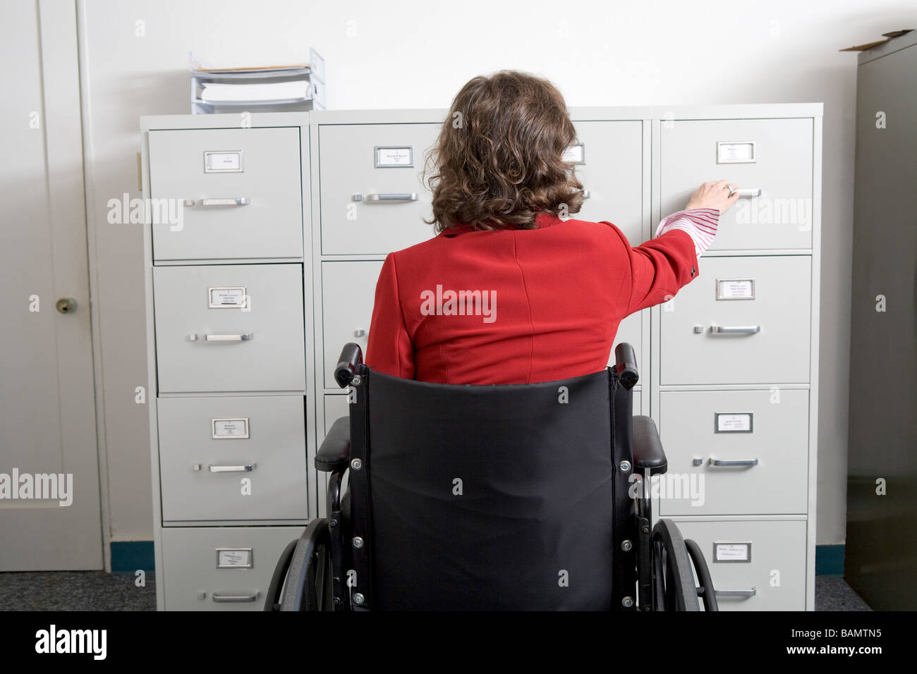 Woman in a wheelchair opening drawer on file cabinet Stock Photo - Alamy