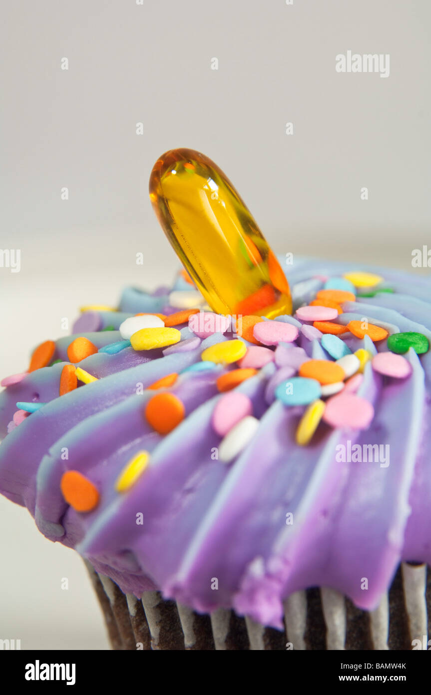 Colourfully decorated chocolate cupcake with vitamin pill inserted into ...