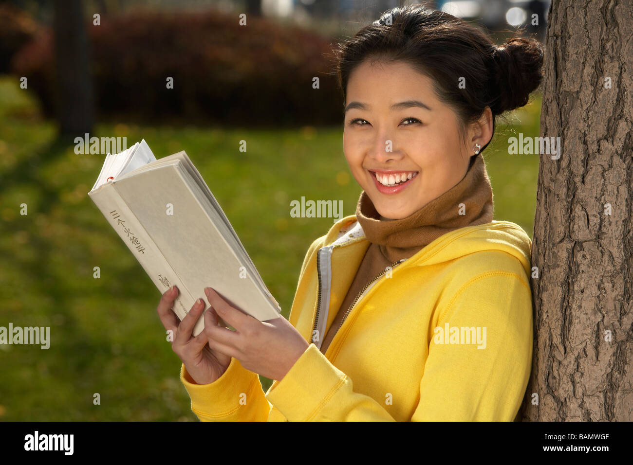 Young Woman Leaning Against A Tree Reading Her Book Stock Photo - Alamy