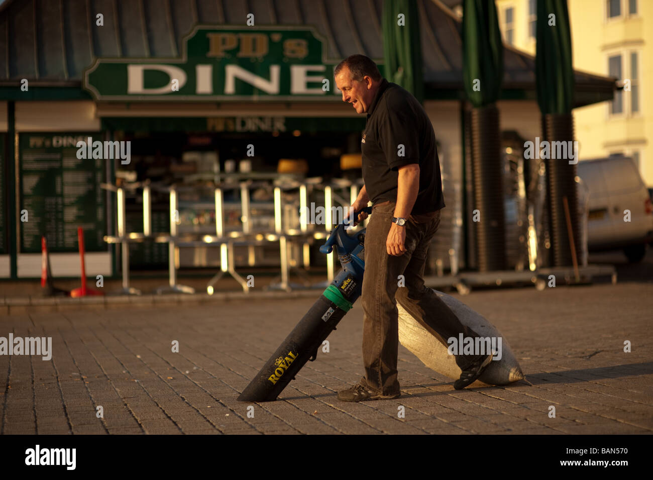 Cafe owner cleaning the pavement outside his diner with an industrial ...