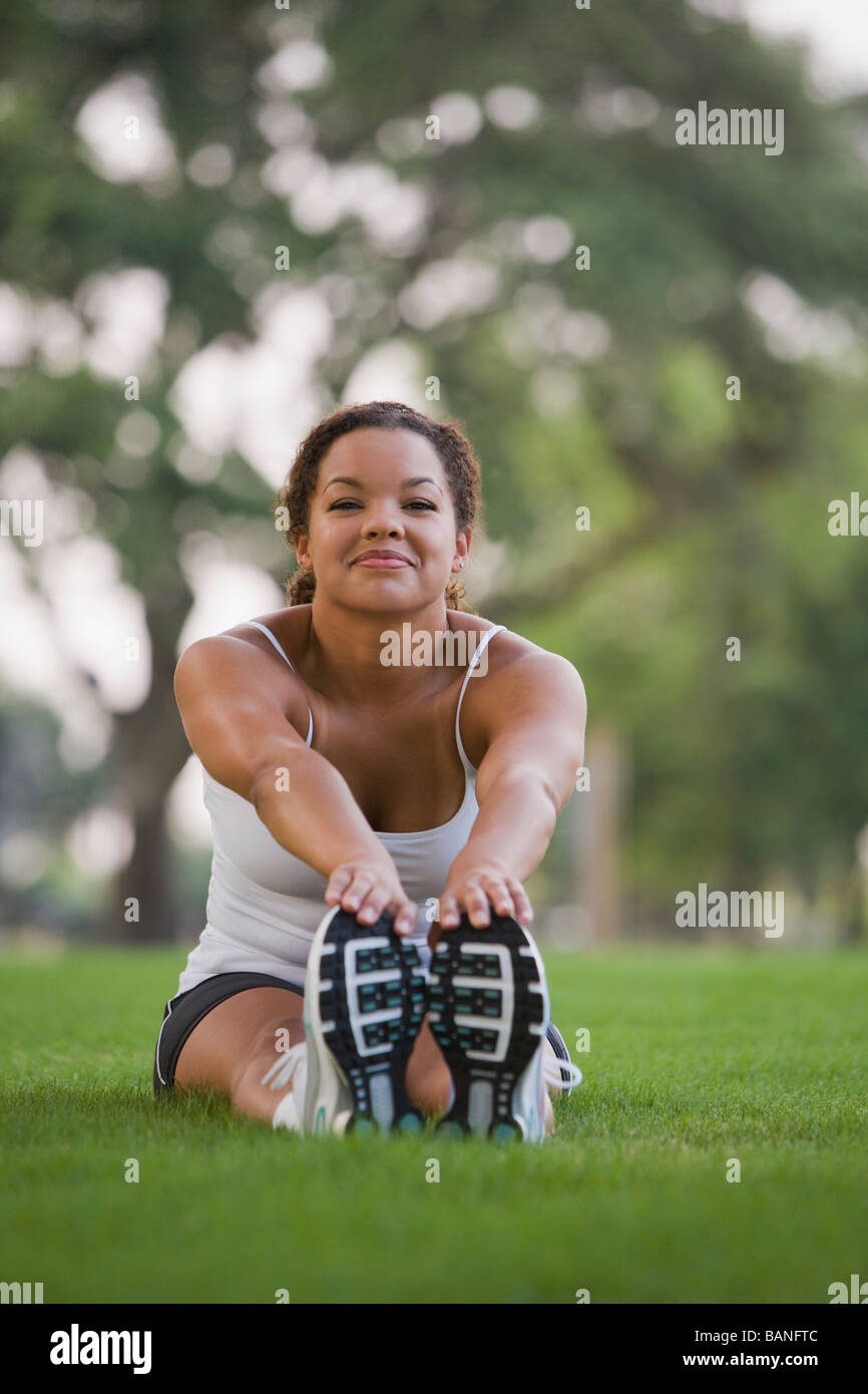 Mixed race woman sitting on grass stretching Stock Photo - Alamy