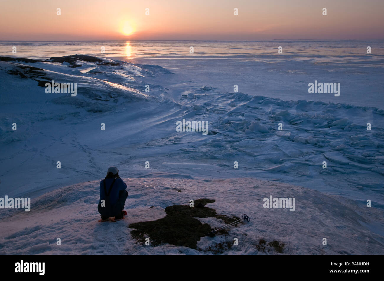 A snowshoeing female admiring sunset over ice covered Lake Superior ...