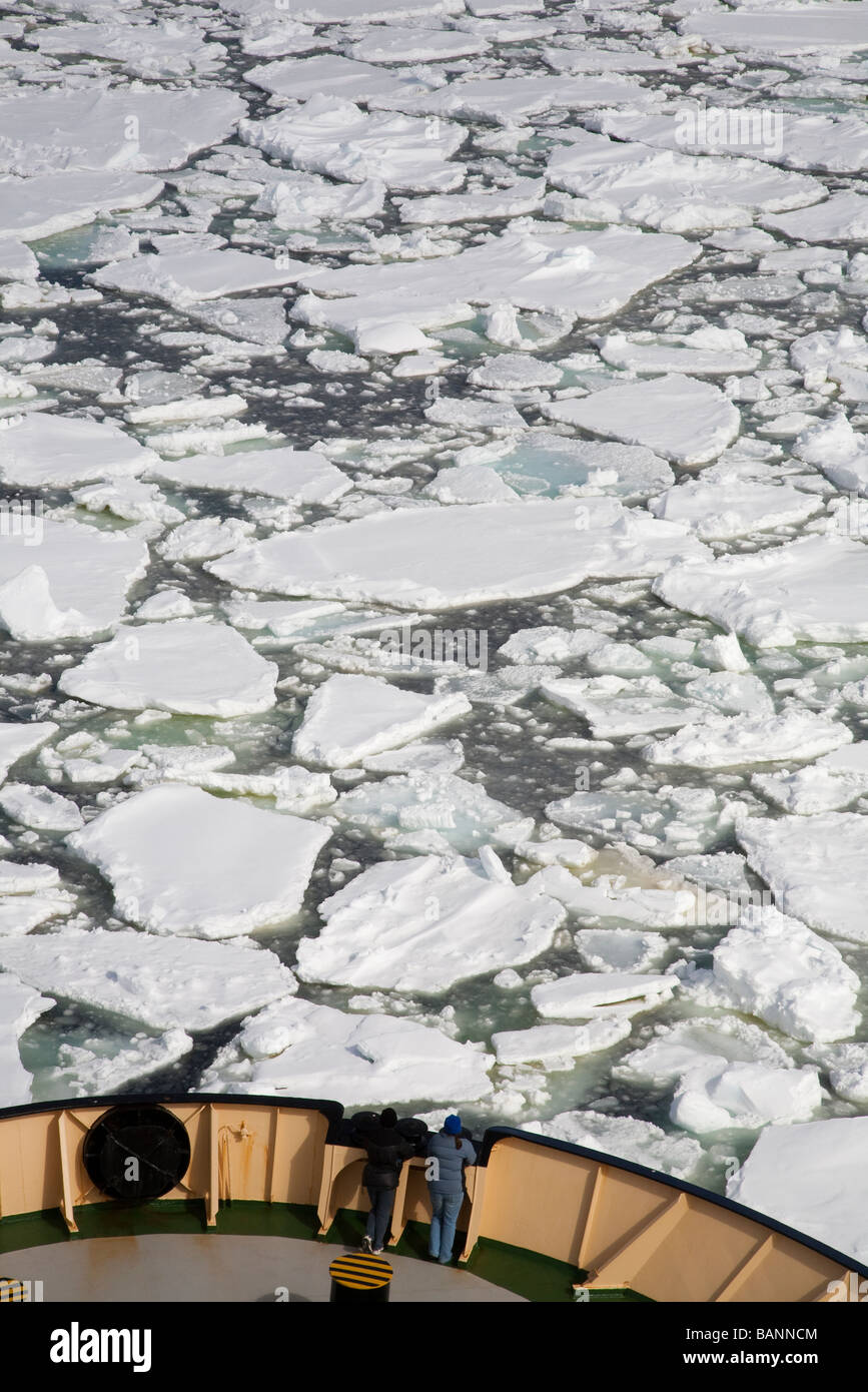 2 people watch from ships deck as icebreaker makes its way through ice ...