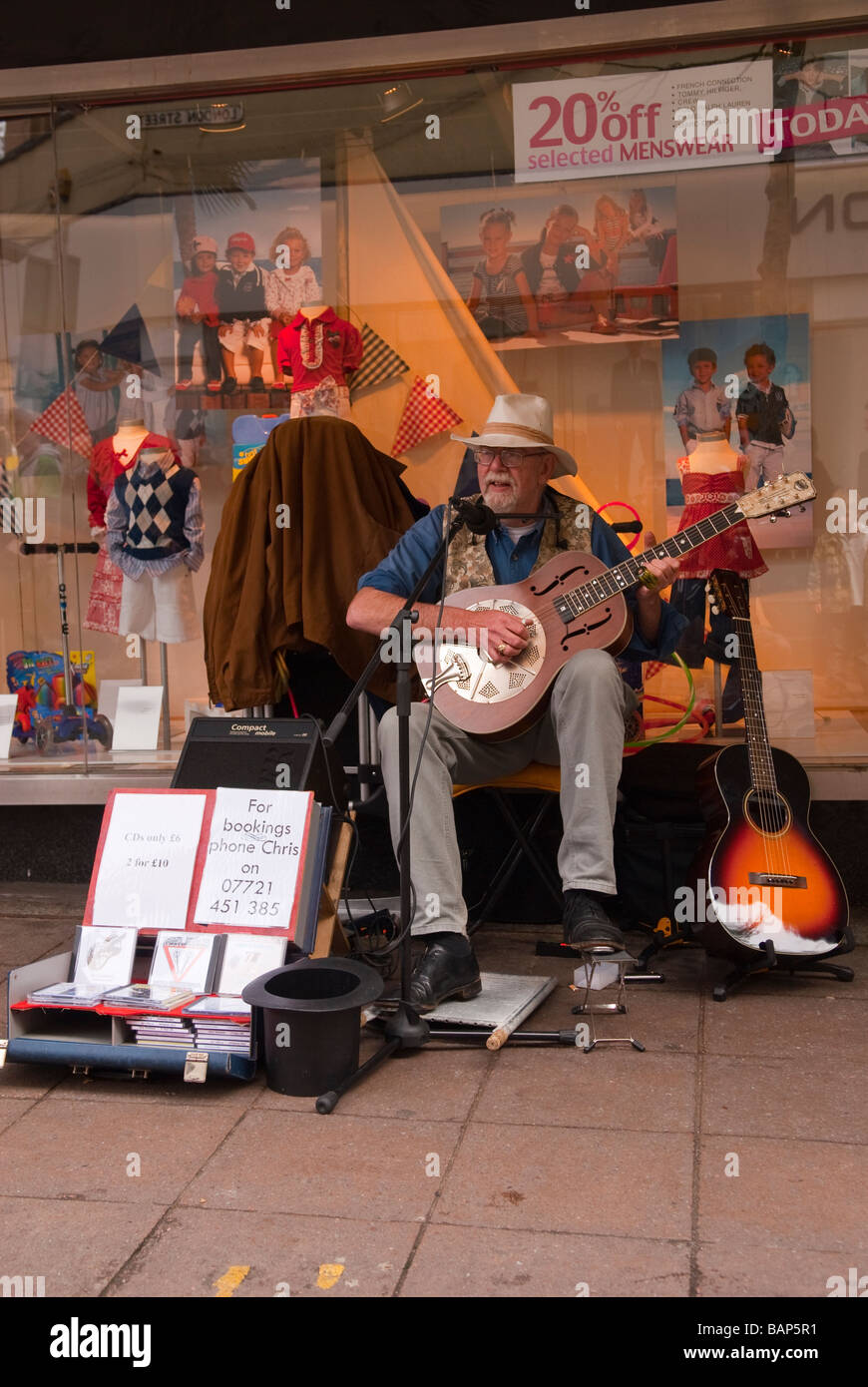 A man busker busking outside a shop with his guitar in a uk city centre ...