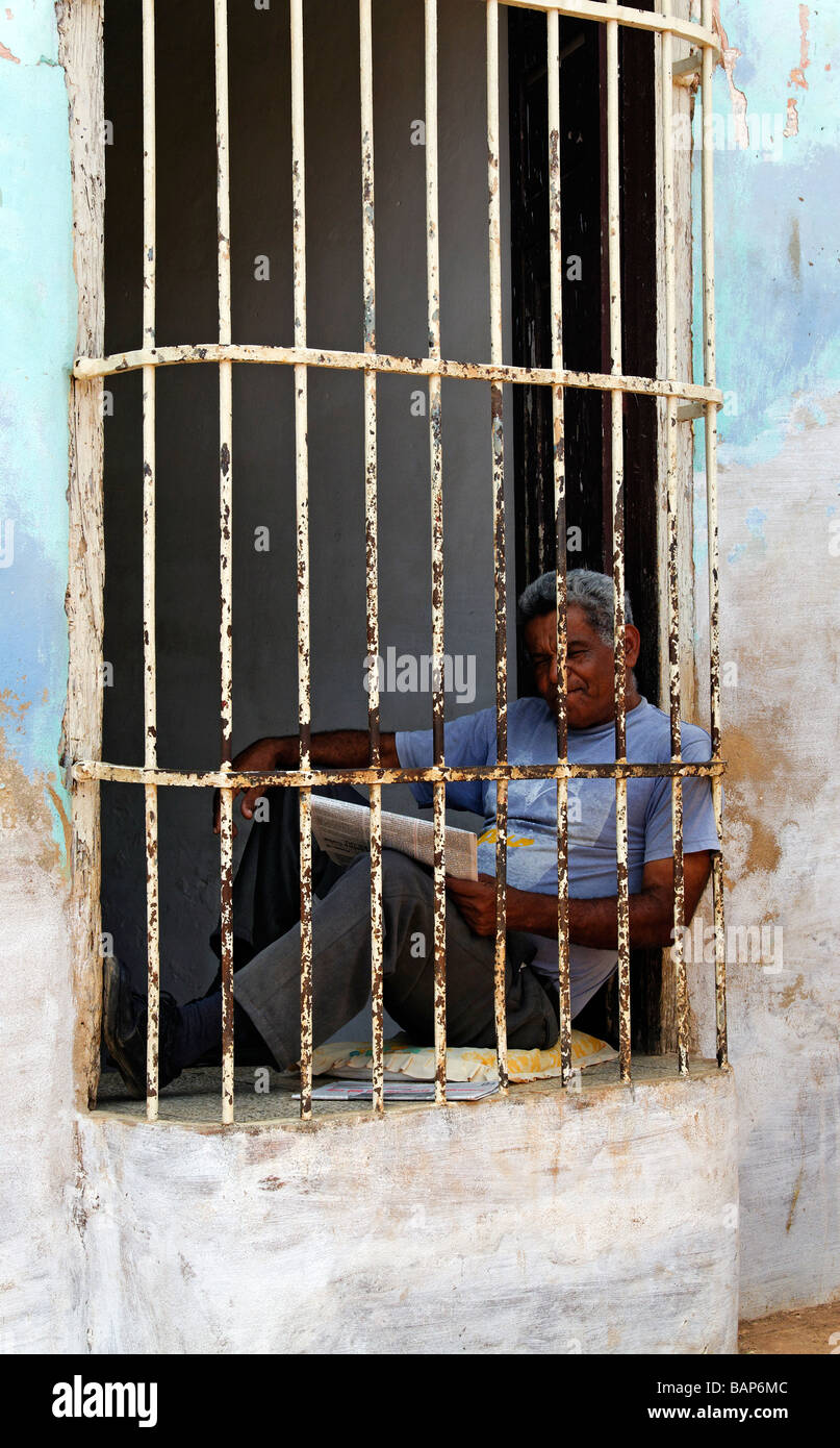 Man reading newspaper in barred window, Trinidad, Cuba Stock Photo - Alamy