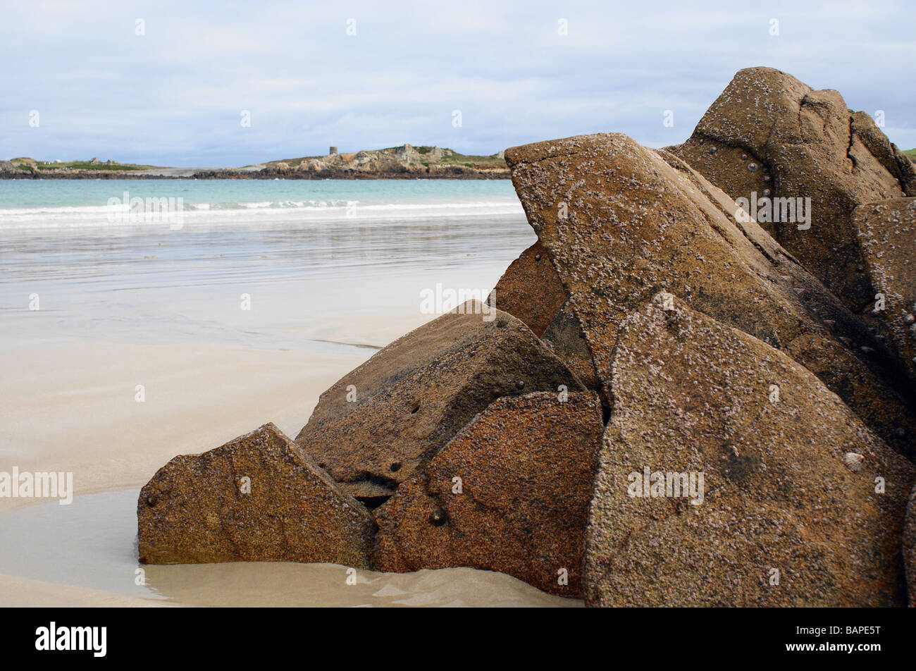 Rocks on a sandy flat beach with the sea rolling in at Guernsey ...