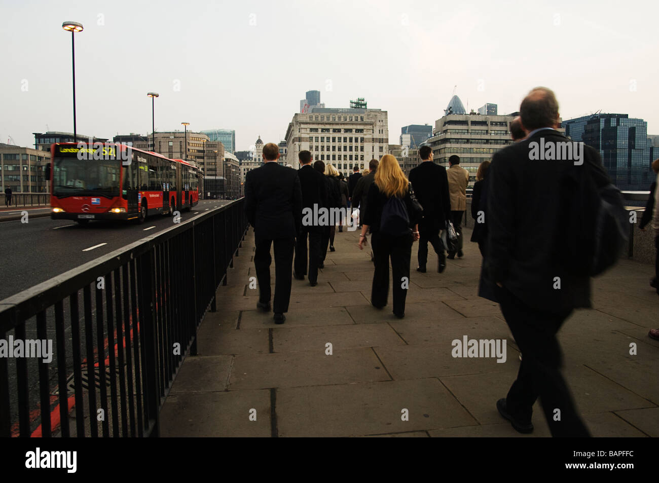 Commuters walking over London Bridge in the morning, with a red London ...