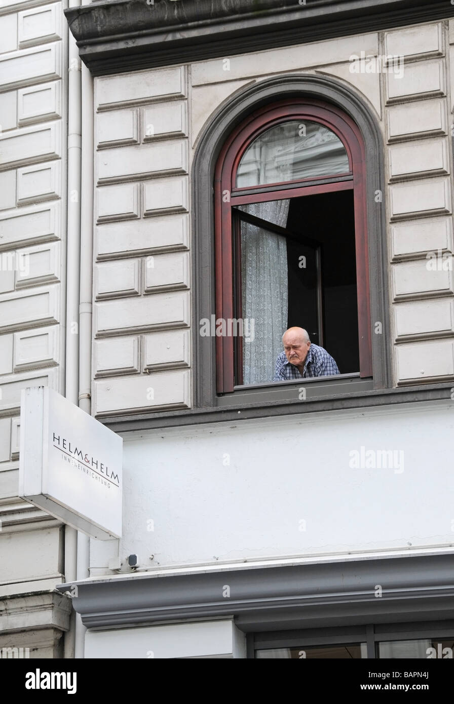 old grimly man looking out of his window in a white house in Ottensen ...
