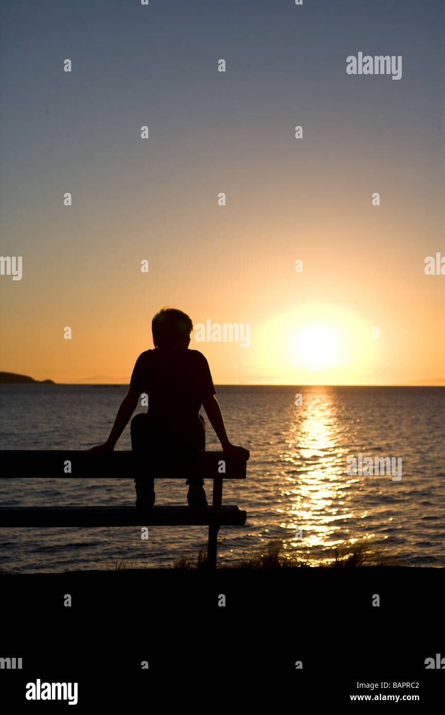 Boy sitting on a bench at sunset in Plimmerton New Zealand Stock Photo ...