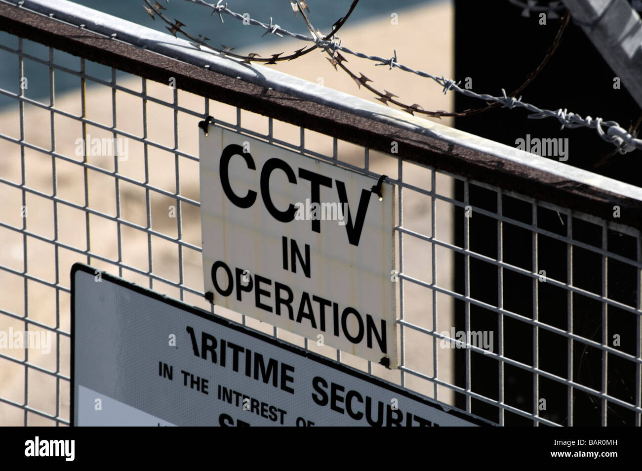 CCTV warning sign and fence topped with barbed wire protecting part of ...