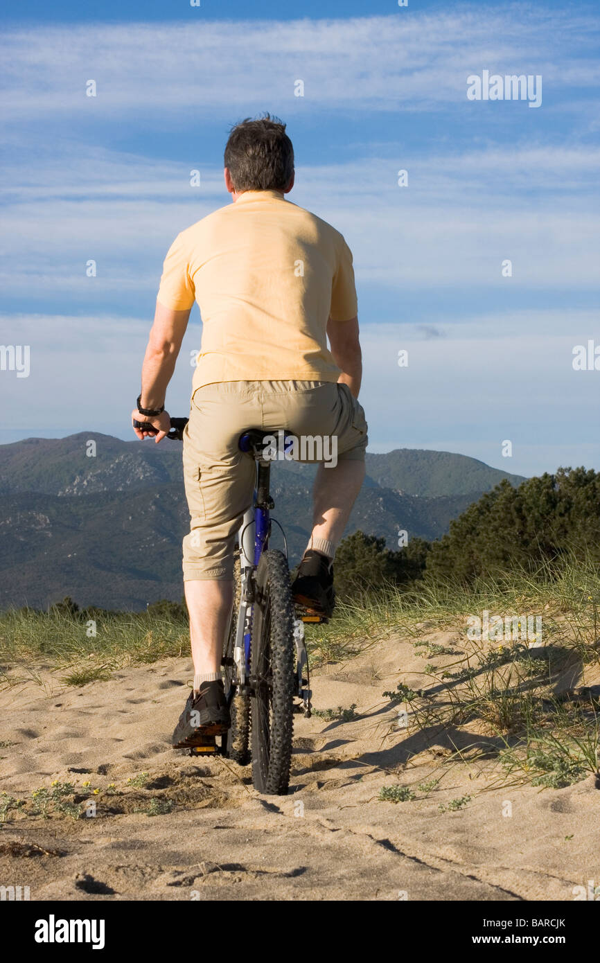 Man riding bicycle on the beach with hills in the background Stock ...