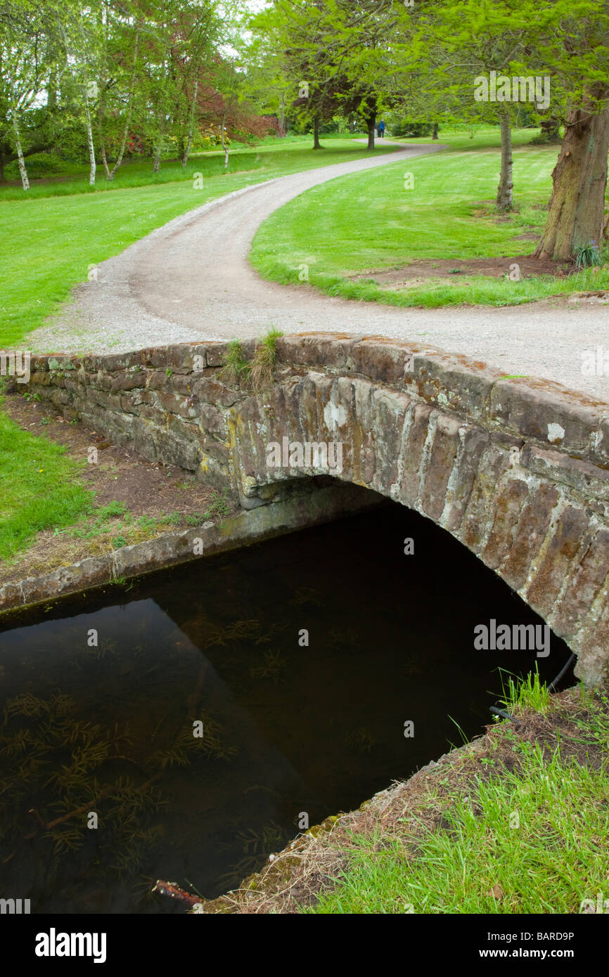 A meandering path and stone bridge over a tranquil slow moving stream ...