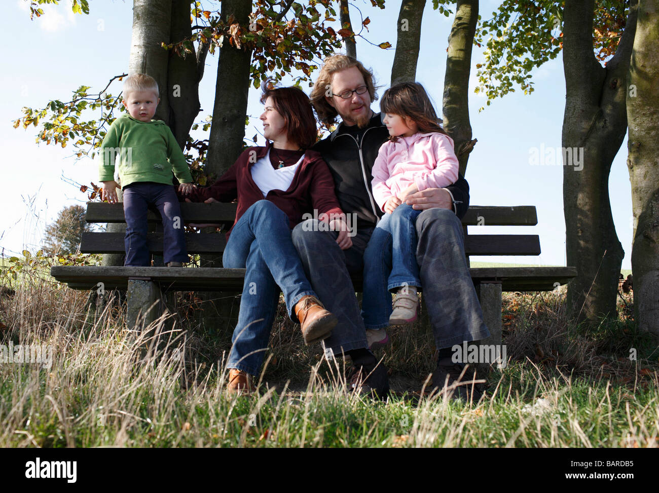 Young family sitting on a bench Stock Photo - Alamy