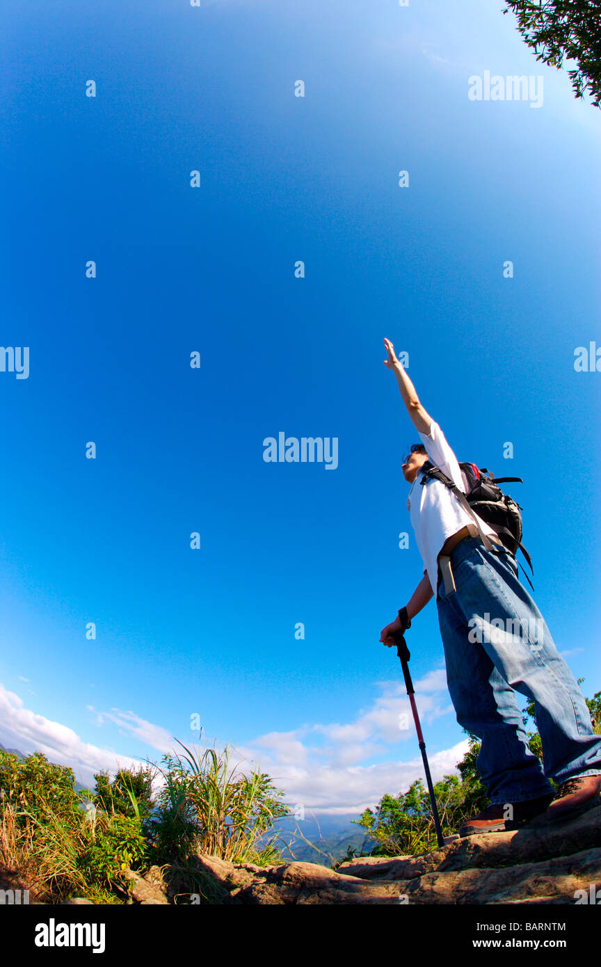 Young man standing on hill reaching arm up against blue sky Stock Photo ...